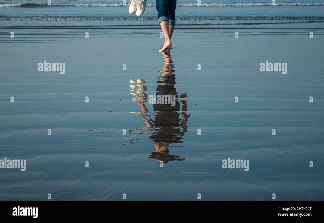 Closeup of reflection of a boy walking on the wet water beach Stock ...