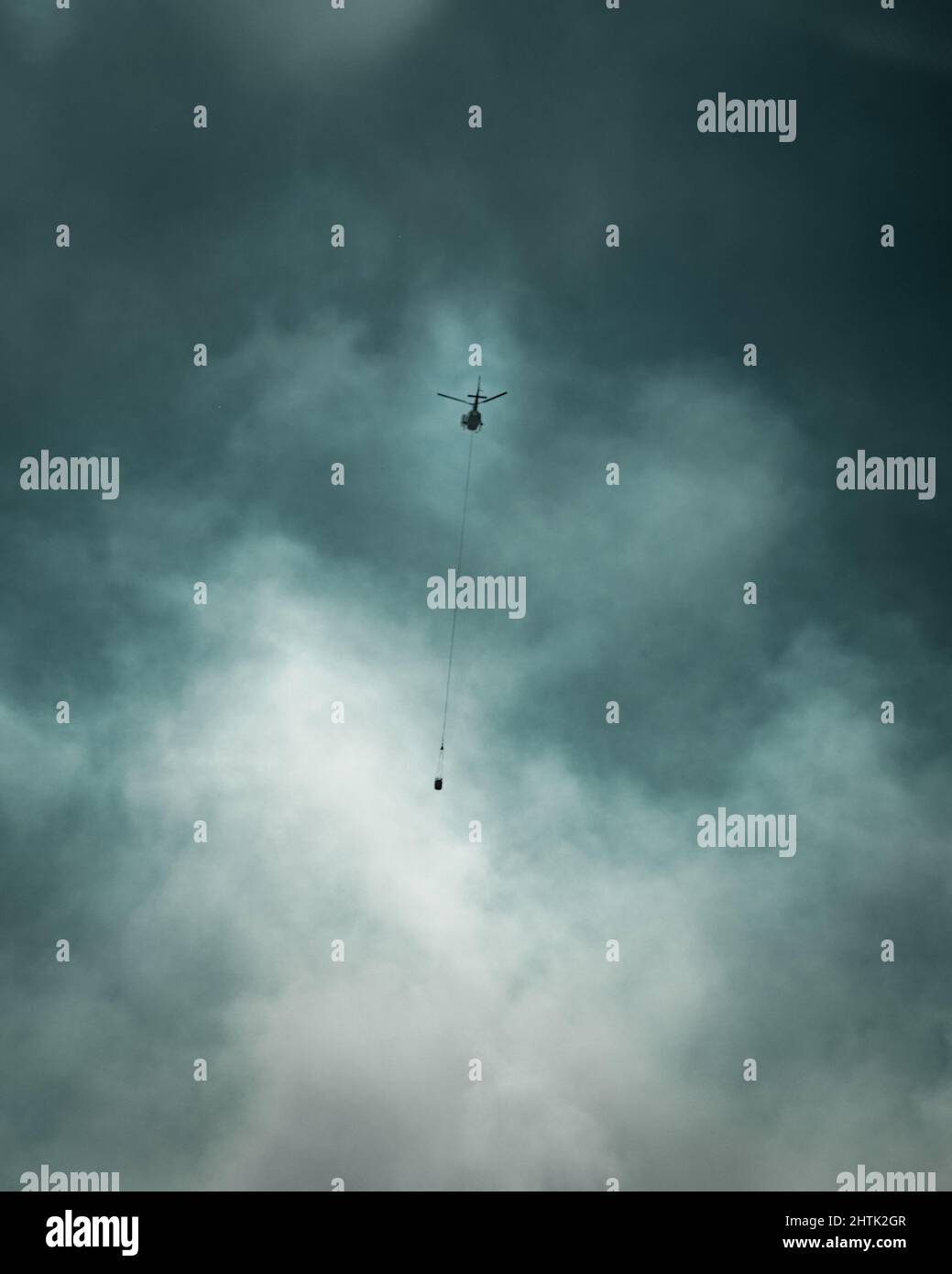 Vertical shot of a helicopter dropping something over a forest in a ...
