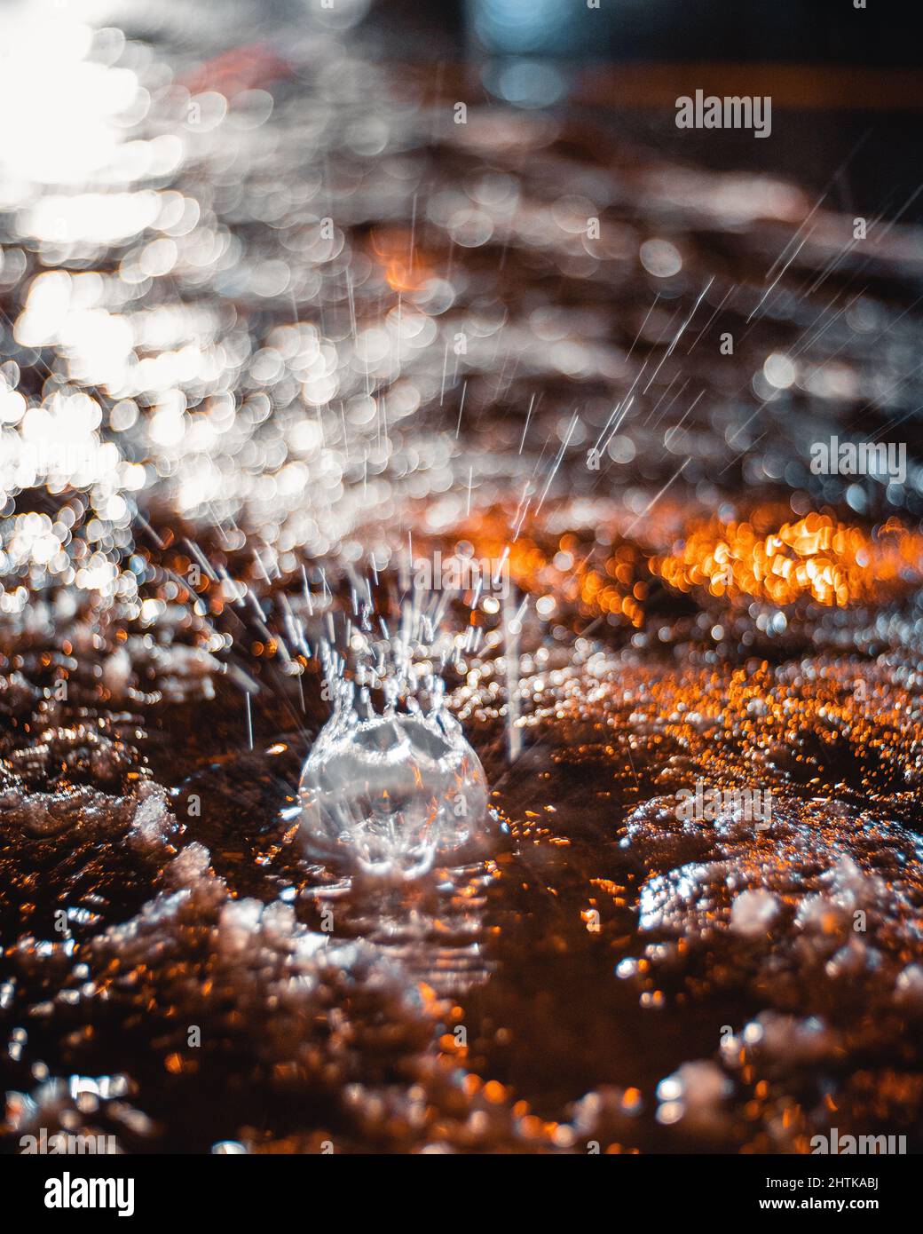 Vertical closeup shot of a raindrop falling on the ground and making a ...