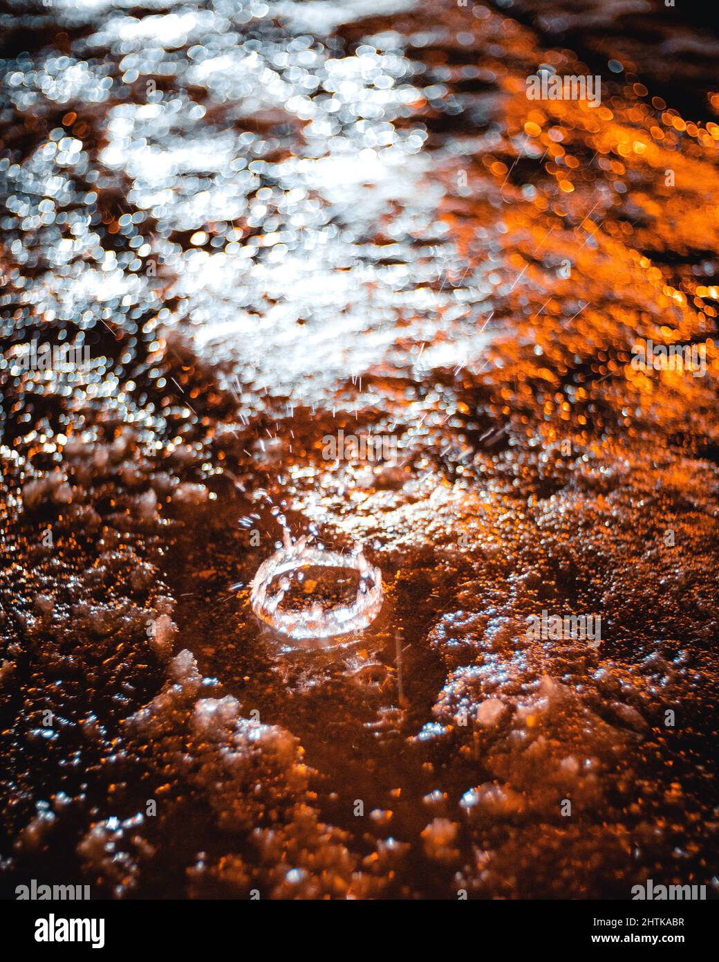 Vertical closeup shot of a raindrop falling on the ground and making a ...