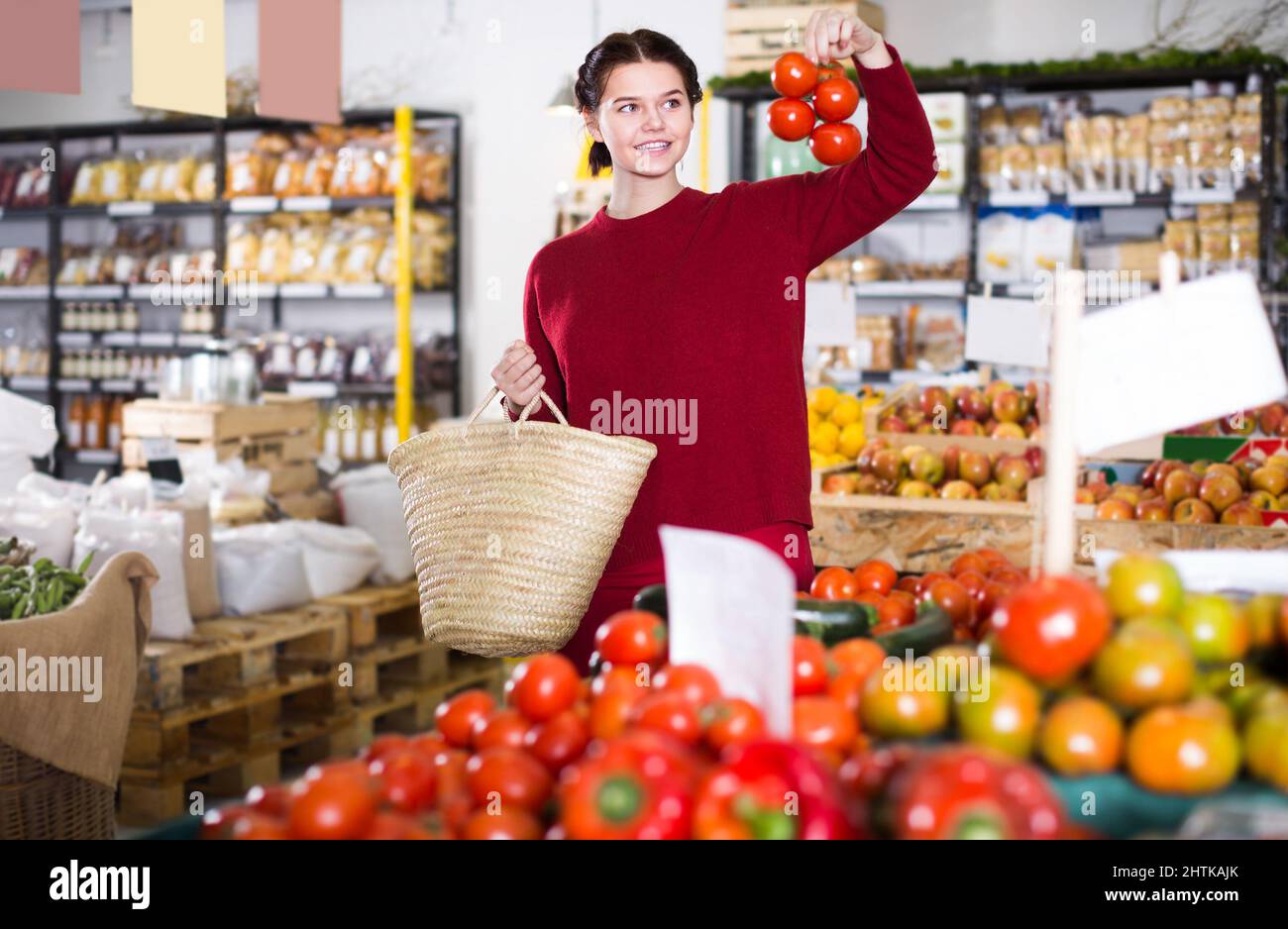 Portrait of cheerful female customer selecting tomatoes in grocery ...