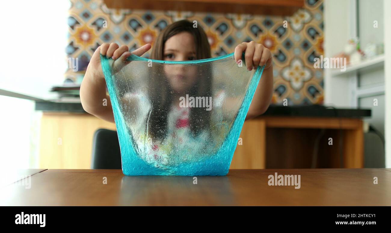 Little girl playing with slimy plasticine creating a bubble with blue ...