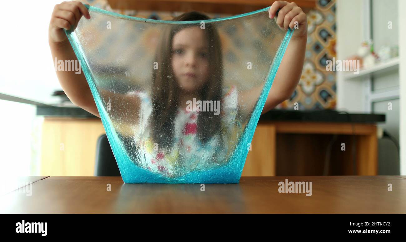 Little girl playing with slimy plasticine creating a bubble with blue ...