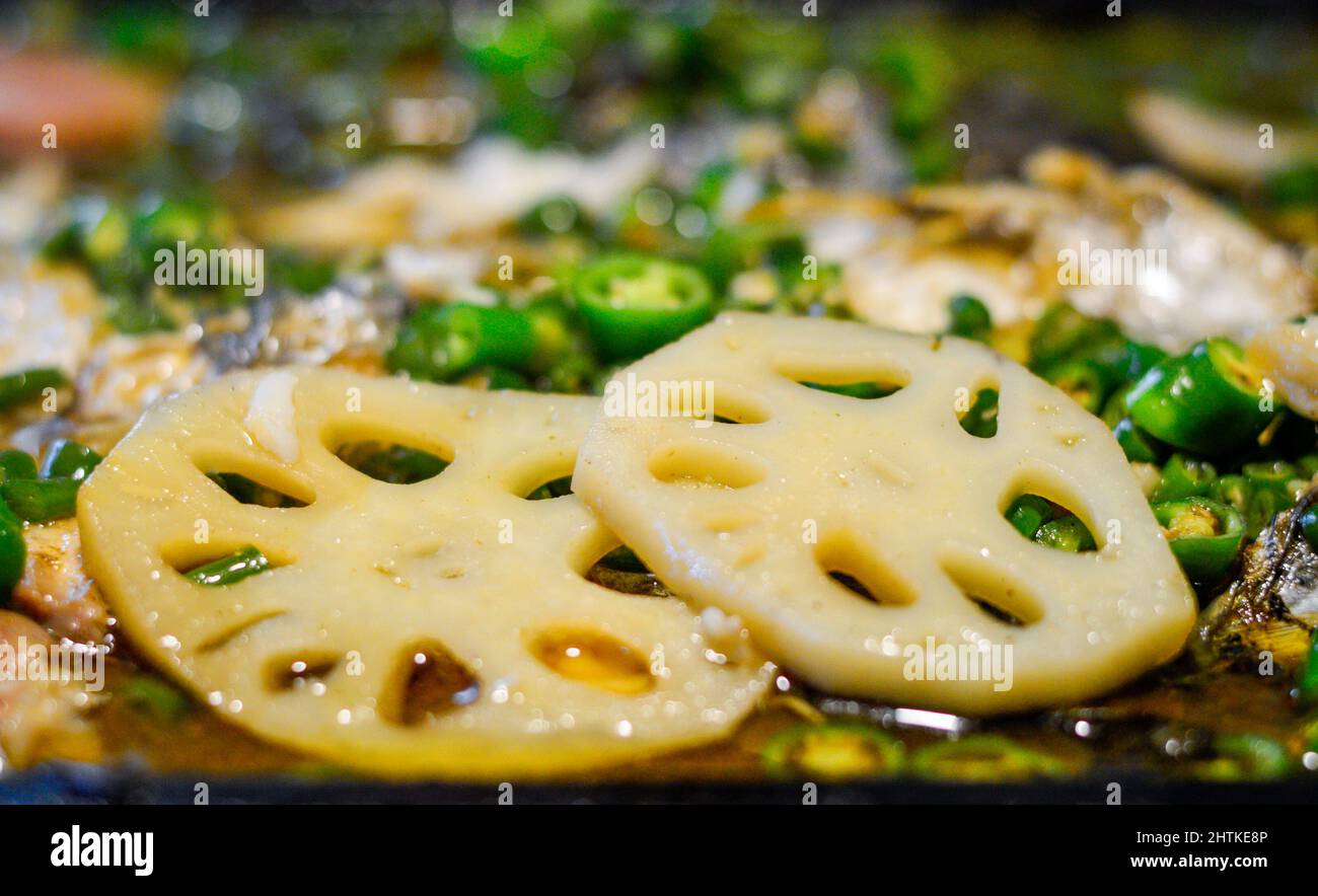 Two slices of lotus root on top of a Chinese hot pot with green chilies ...