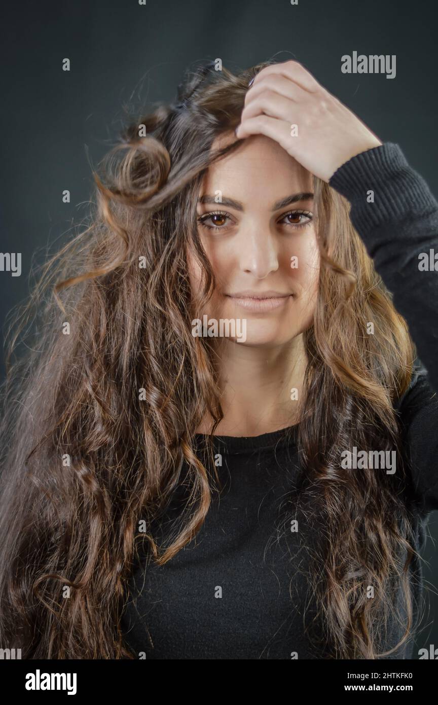 Portrait of a beautiful young woman who tries to fix her very long hair ...