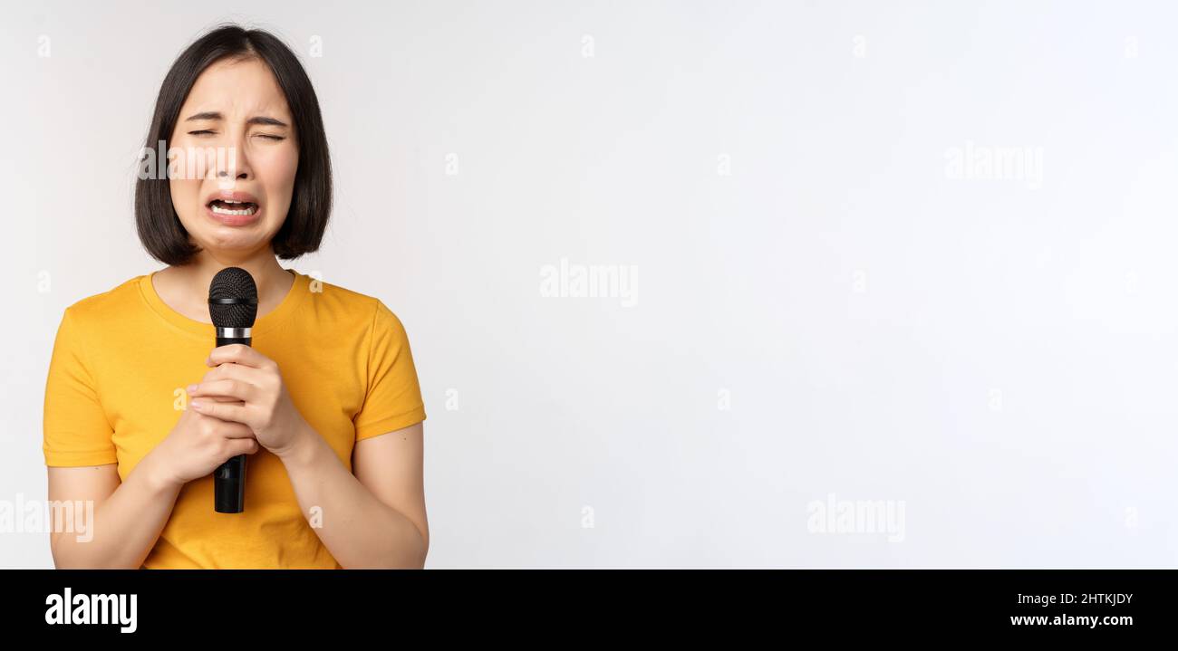 Crying asian girl singing heartbroken in microphone, holding mic and ...
