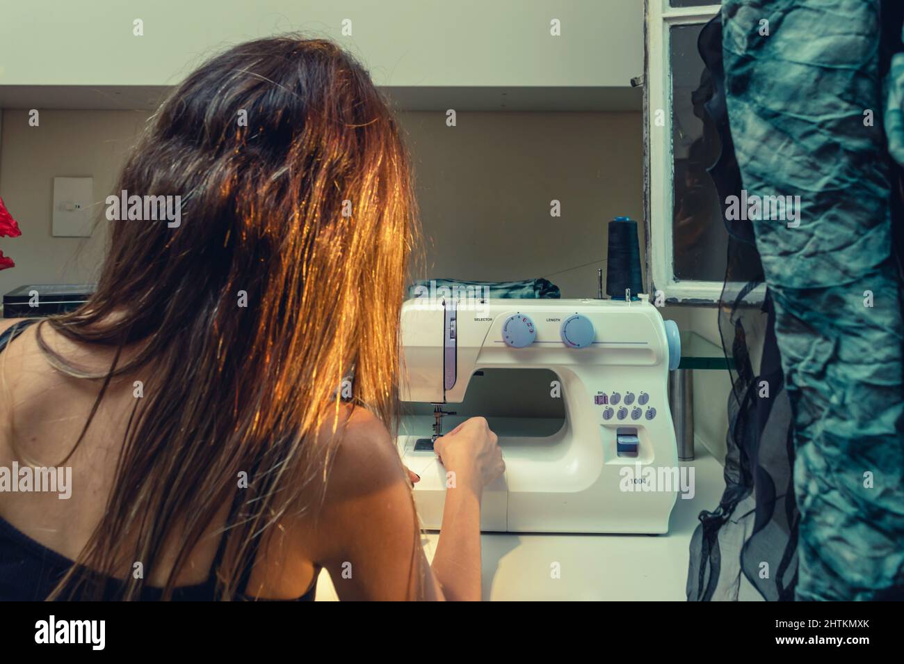 rear view of a woman threading a dark blue thread in the needle of her ...