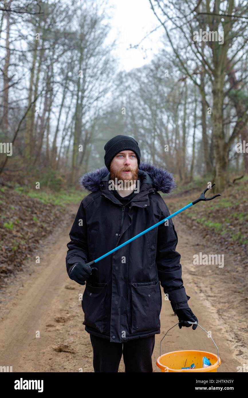 A portrait of a young bearded man with a litter picker and a bucket ...