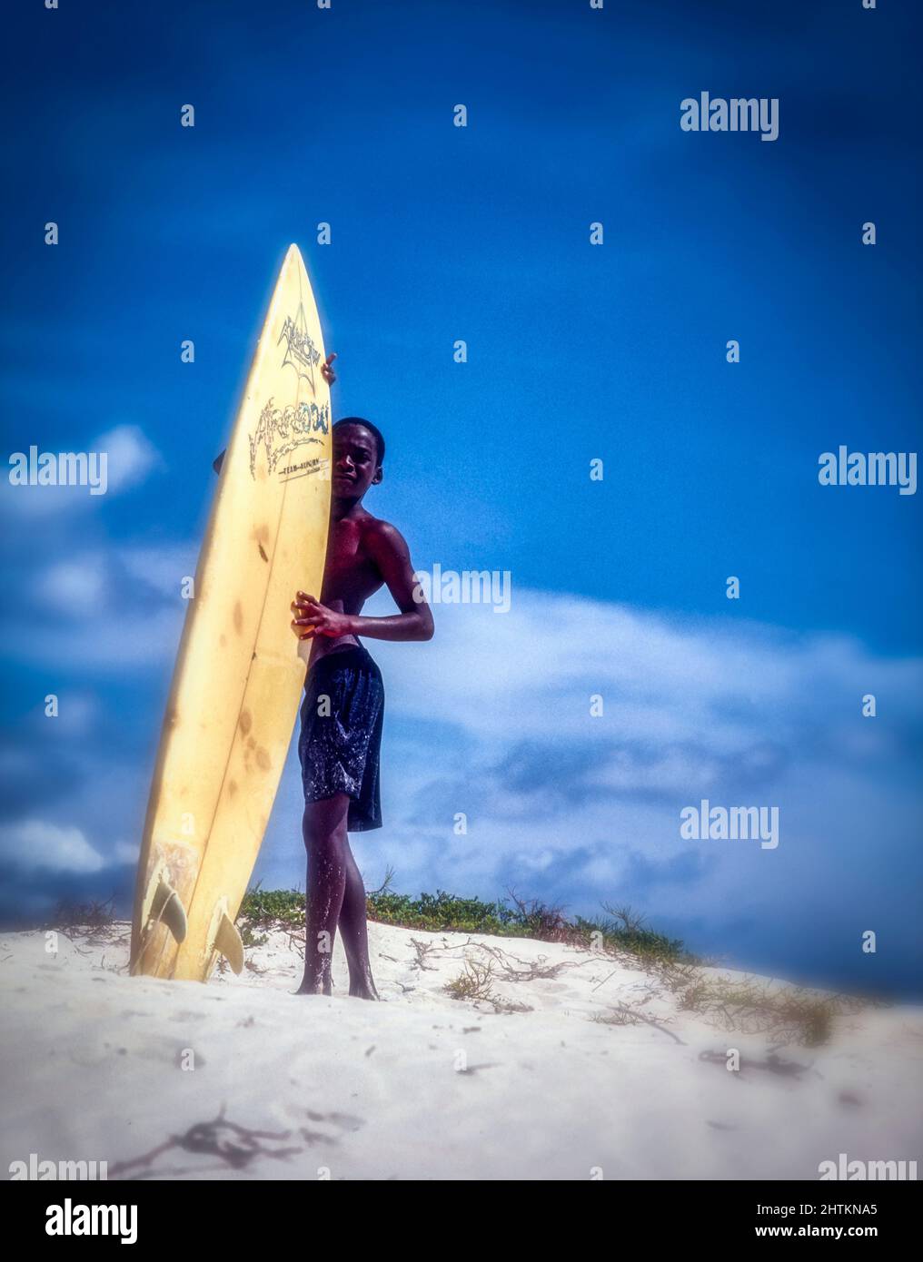 Adolescent black surfer with his board on a white sand Barbados beach ...