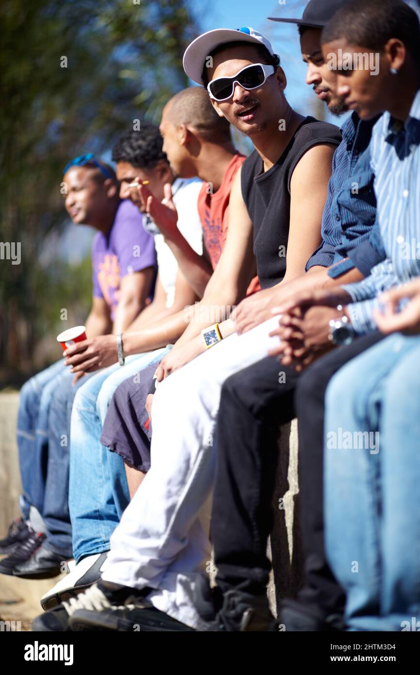 Just hanging out. Shot of a group of friends sitting on a wall together ...