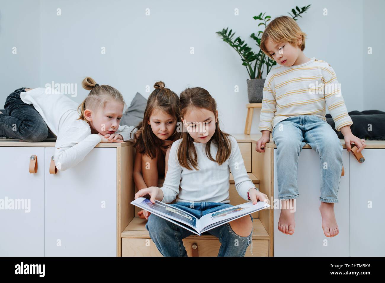 Bored children gathered in a room to read a picture book, all looking ...