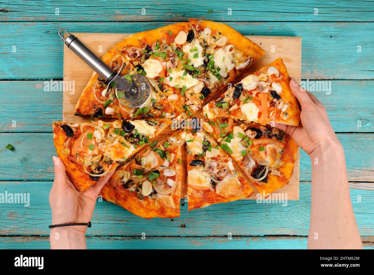 Homemade round pizza with sea food in woman's hands on turquoise table ...