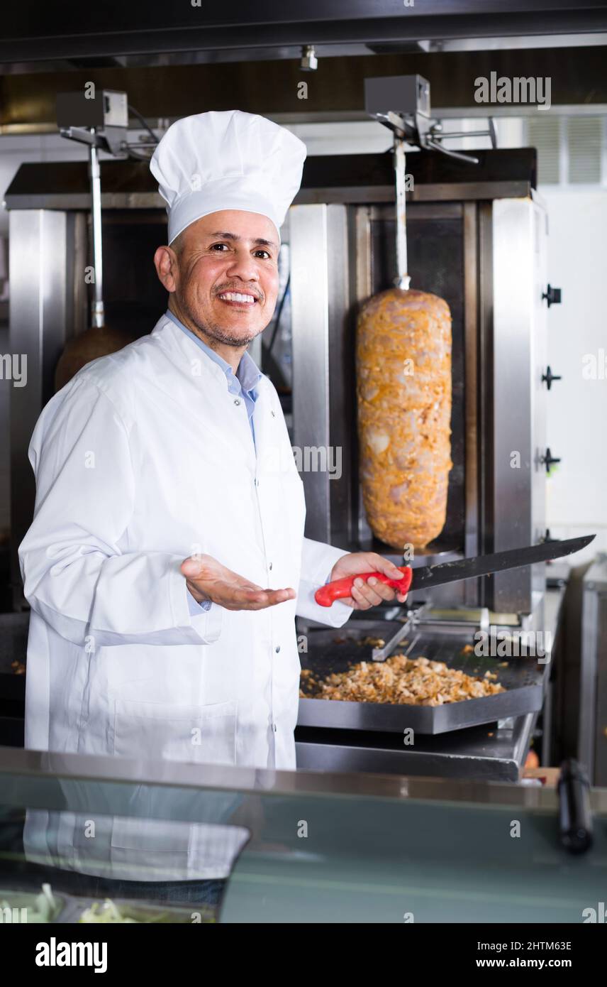 man chef wearing uniform cutting meat for kebab on kitchen in fast food ...
