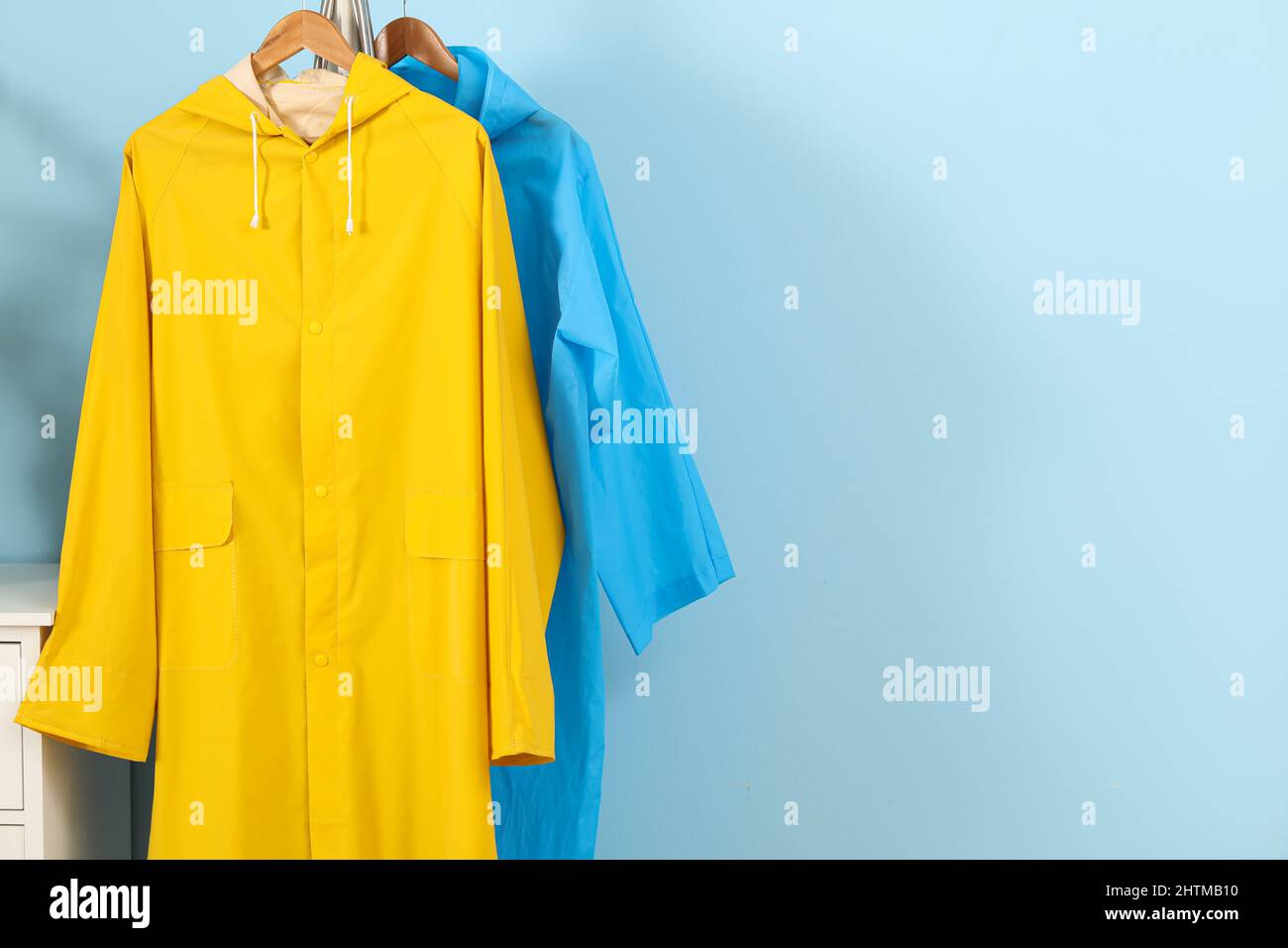 Raincoats hanging on rack near blue wall Stock Photo - Alamy