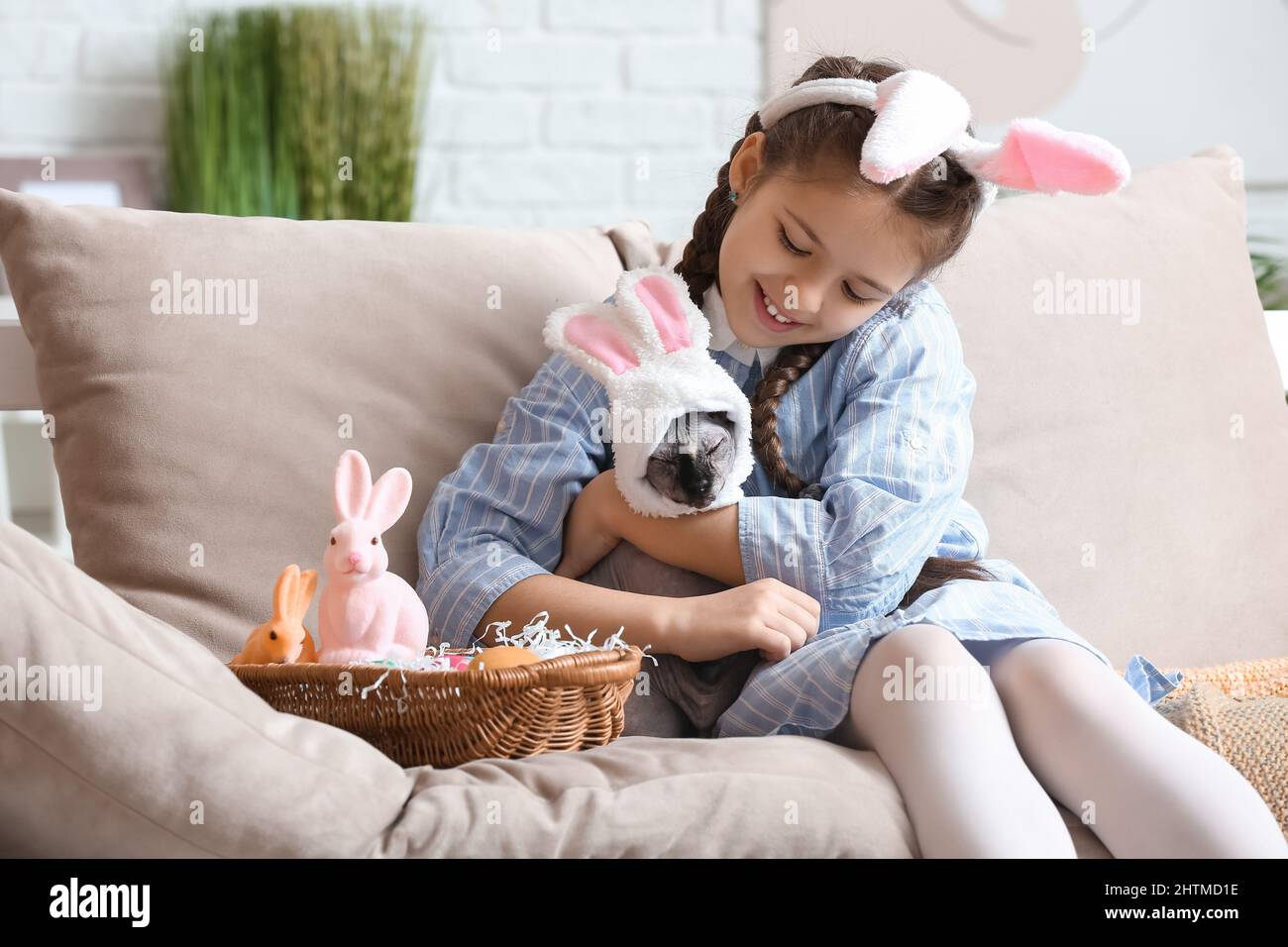 Little girl with Sphynx cat, Easter eggs and rabbits on couch at home ...