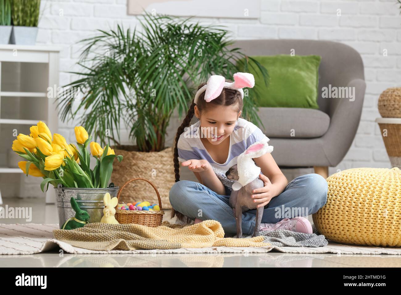 Little girl with Sphynx cat, Easter eggs, rabbits and tulips at home ...