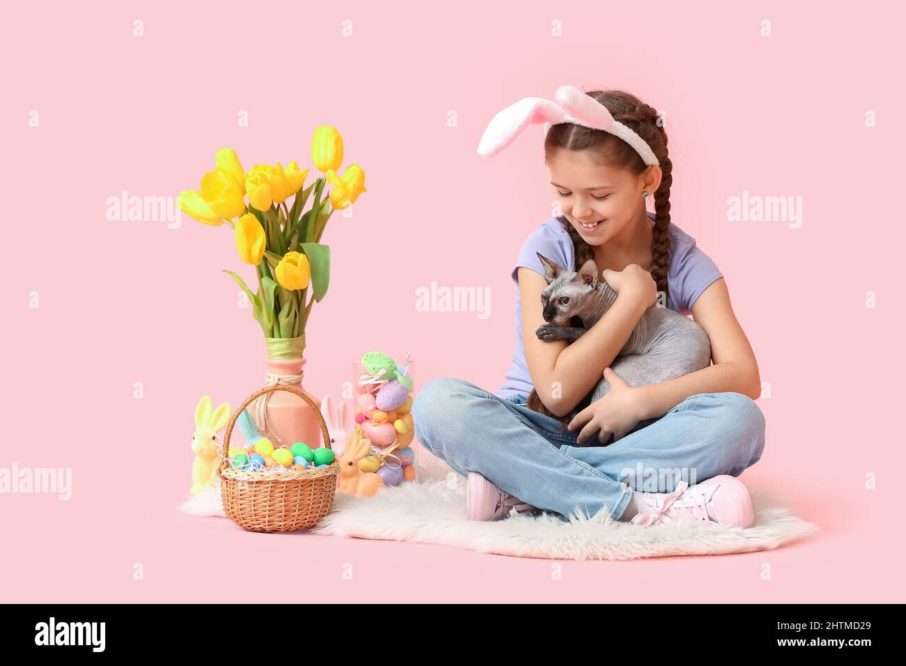 Little girl with Sphynx cat, Easter eggs, rabbits and tulips on pink ...