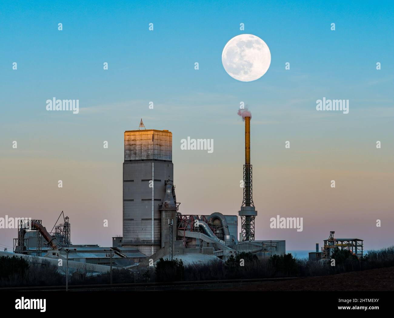 Full moon rising over industrial buildings and steam cooling tower at ...