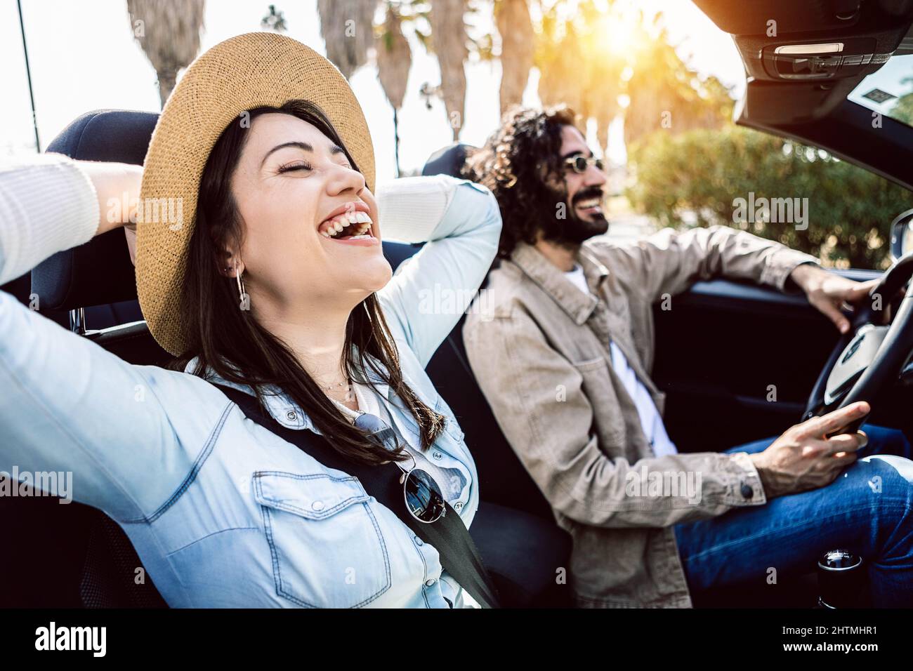Happy young couple laughing together while driving a convertible car on ...