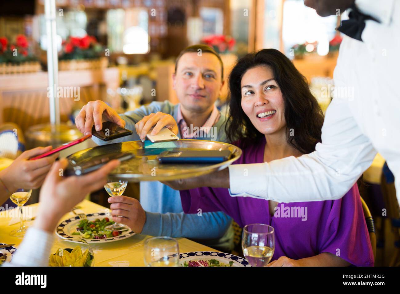 African american waiter collecting phones of cheerful company in ...