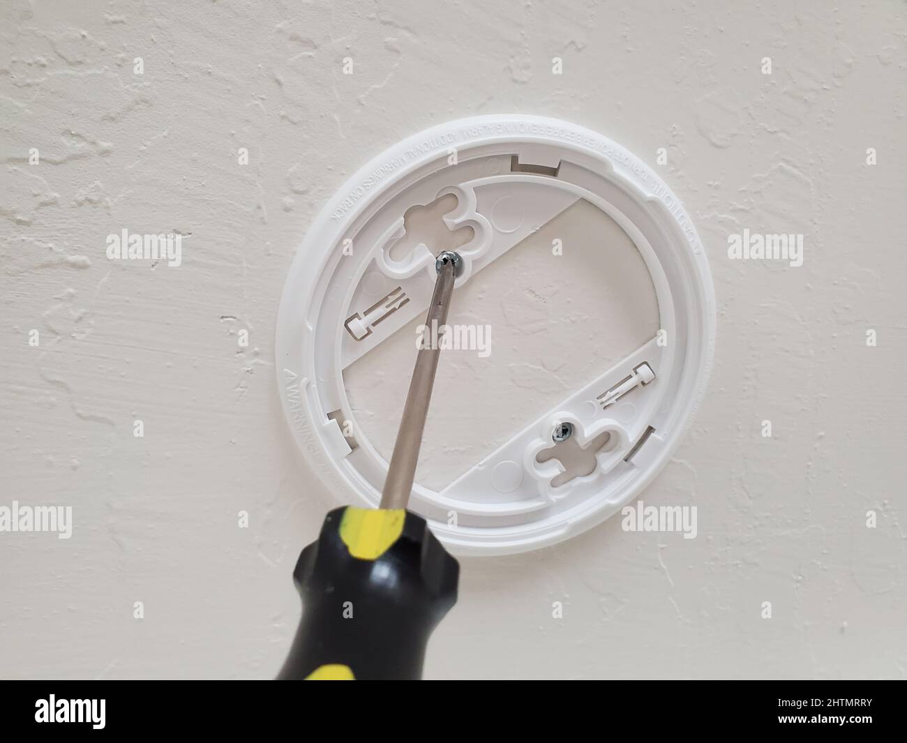 A screwdriver is used to install the mounting plate for a smoke alarm ...