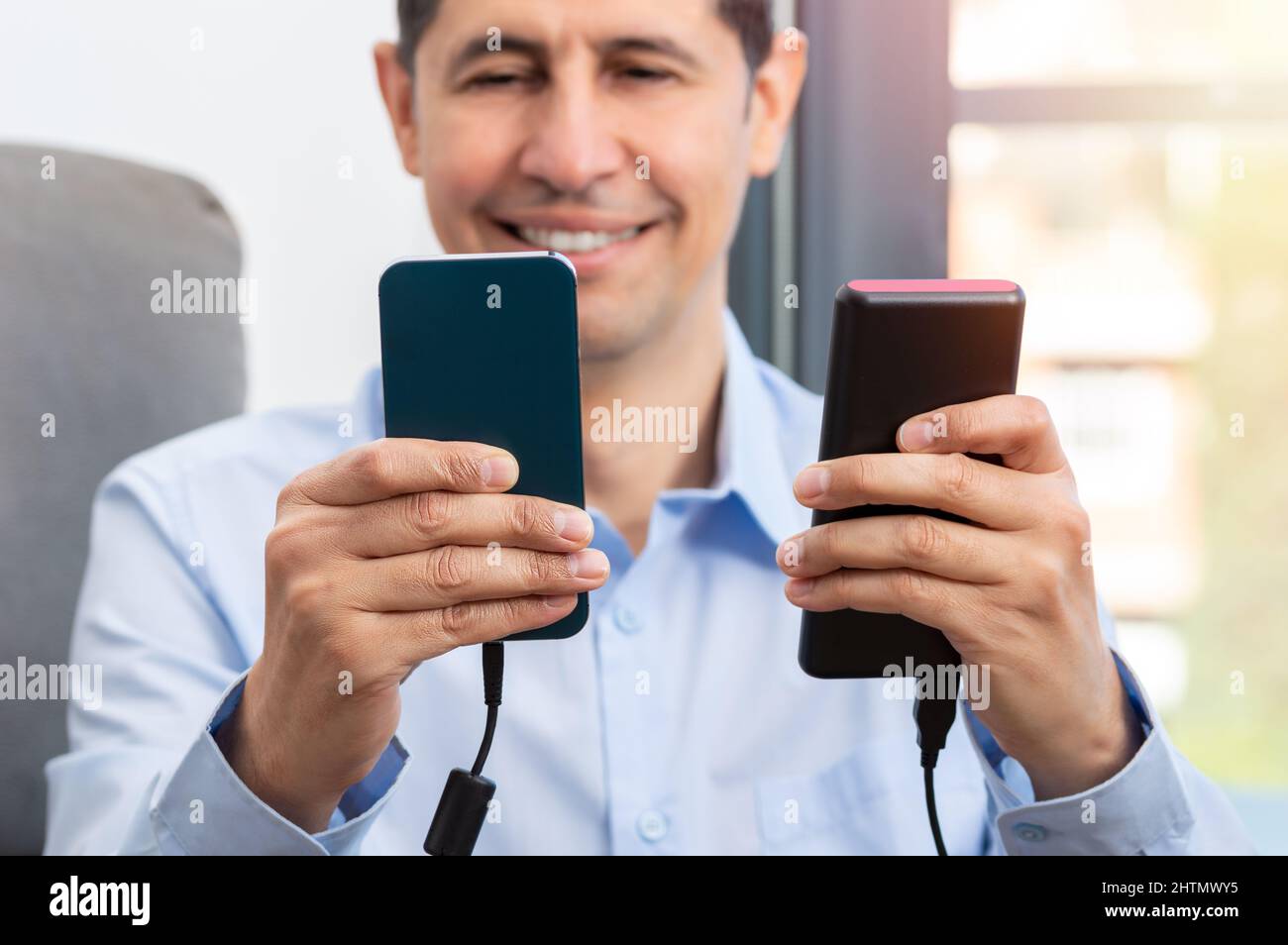 Close-up of happy man charging a smartphone with a portable charger ...