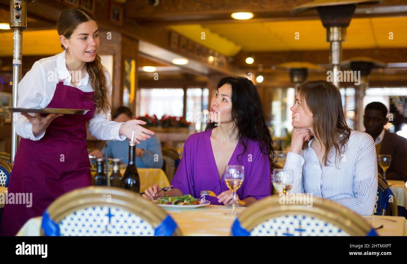 Attentive young waitress talking to female guests in restaurant Stock ...