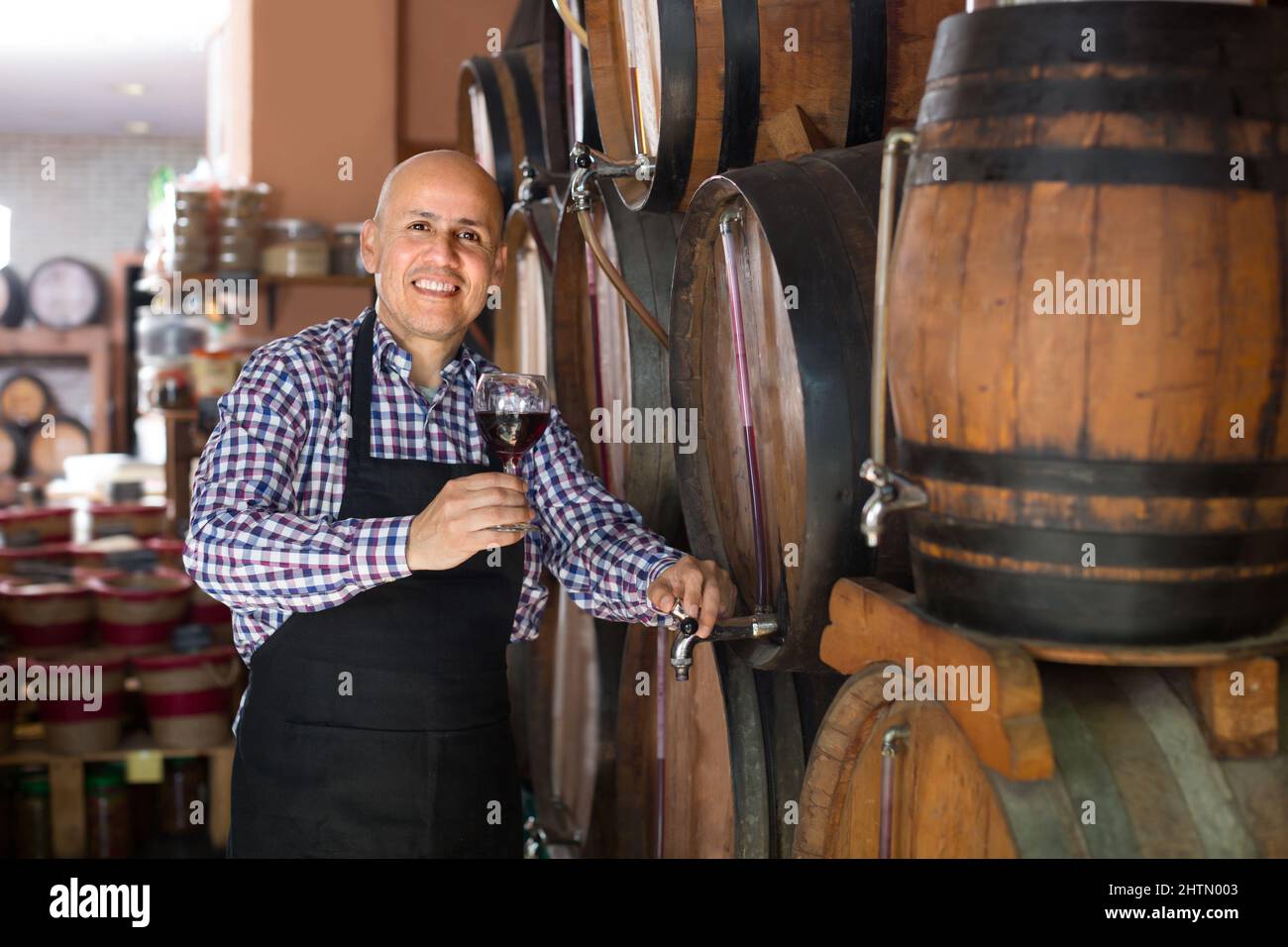 Smiling male wine maker taking wine from wood Stock Photo - Alamy