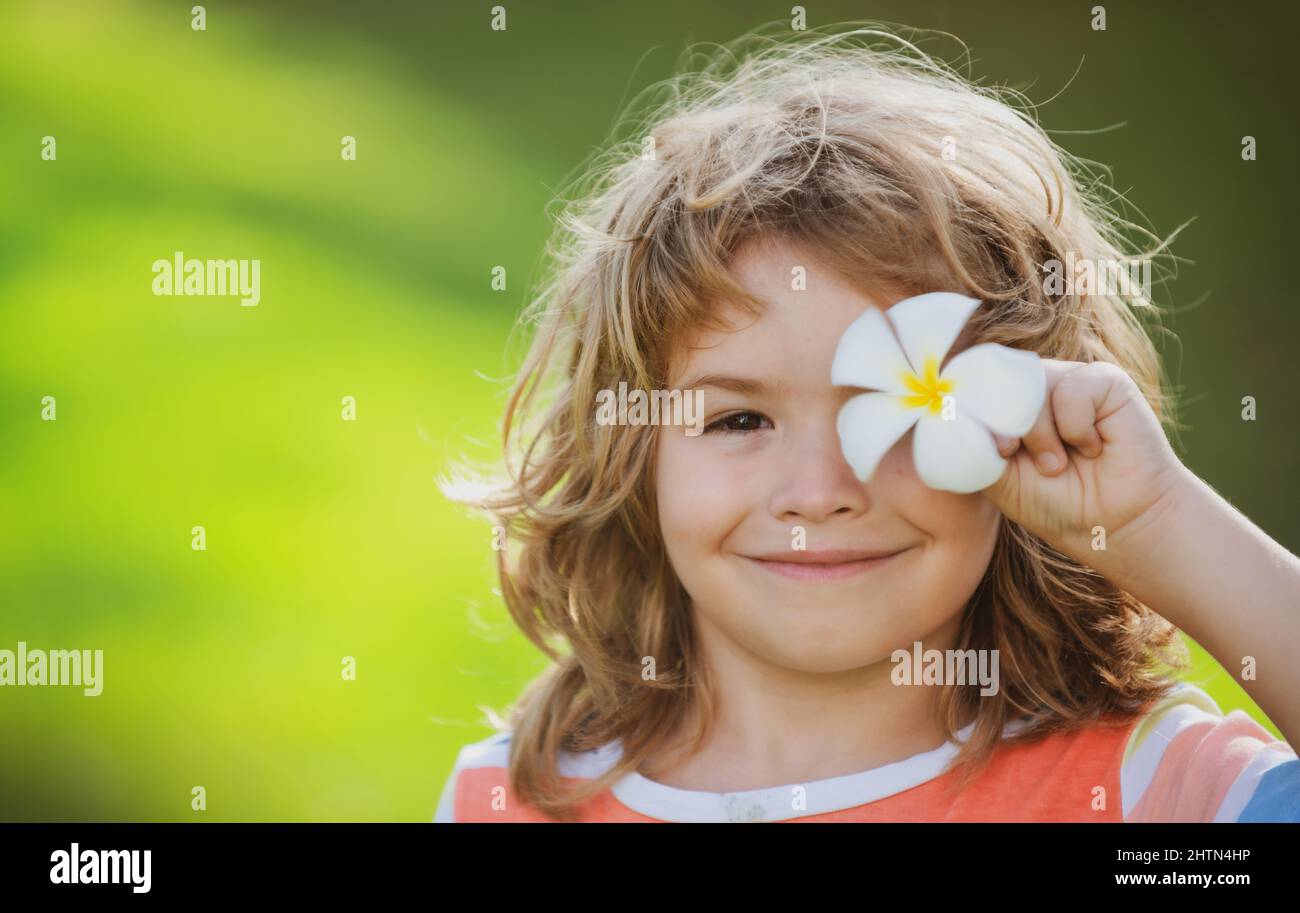 Close up portrait of a small blond boy eyes plumeria flower. Funny kids ...