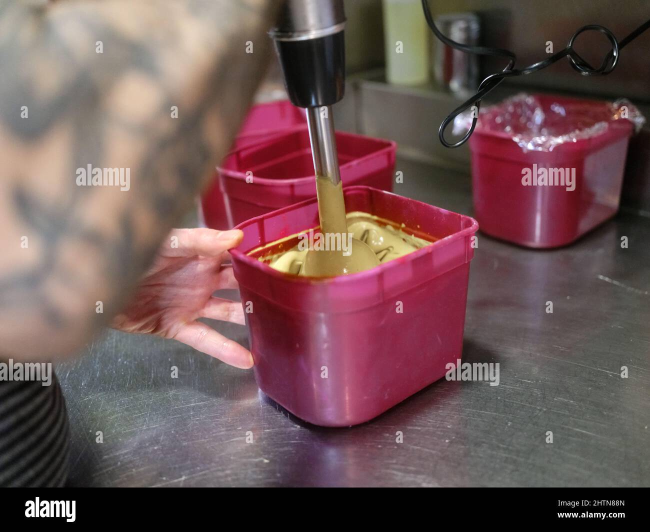 Chef using an electric mixer to remove sauce in a plastic container in ...