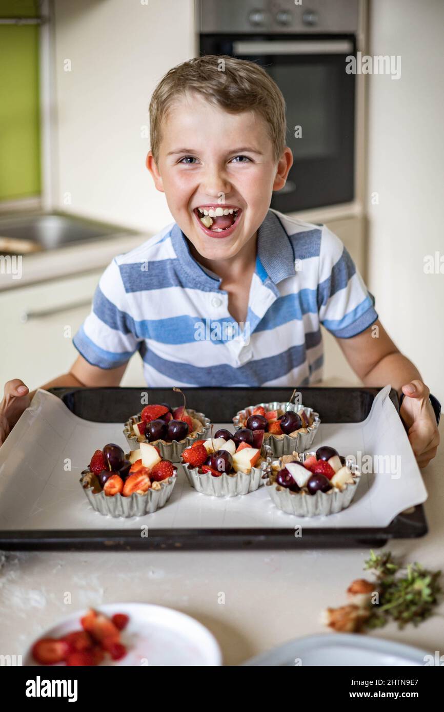 Portrait of happy baby boy posing with baking sheet full of summer ...