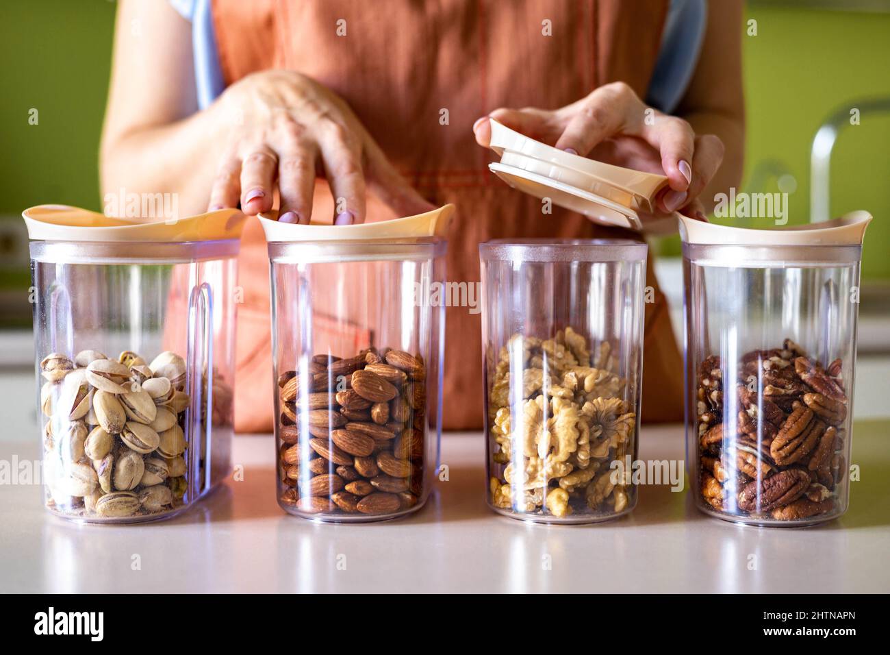 Closeup woman hands in apron placing different nuts into glass jar ...