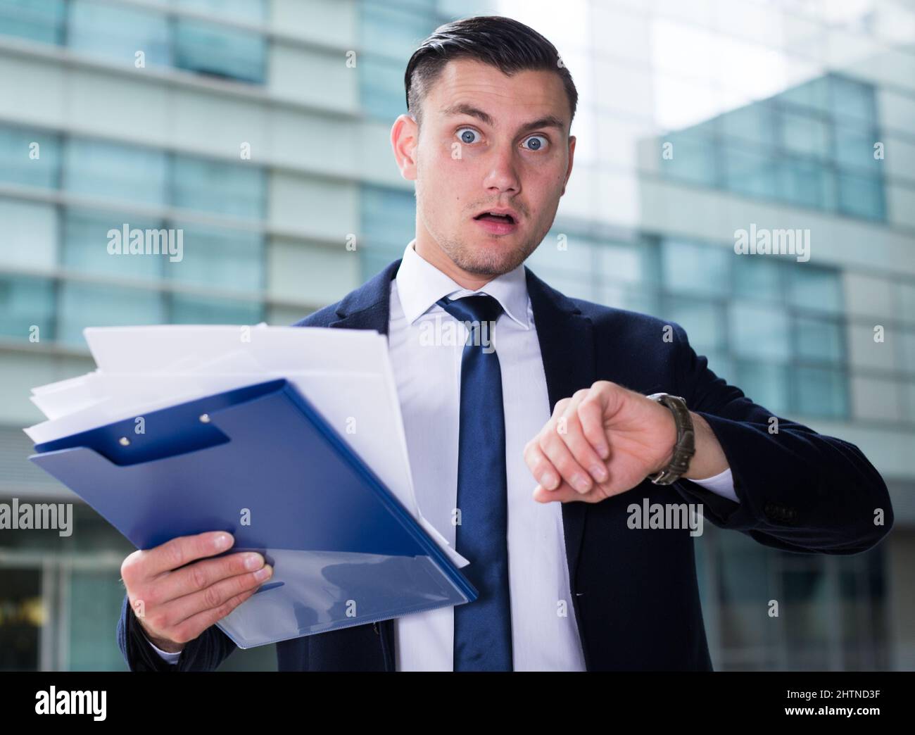 Man in suit is looking on watch near the office Stock Photo - Alamy