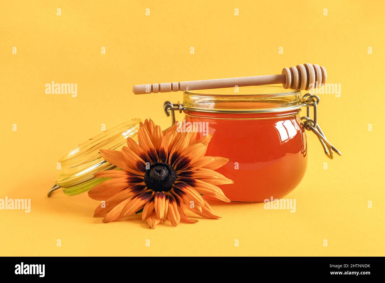 Glass jar of natural honey with wooden drizzler and rudbeckia flower on ...