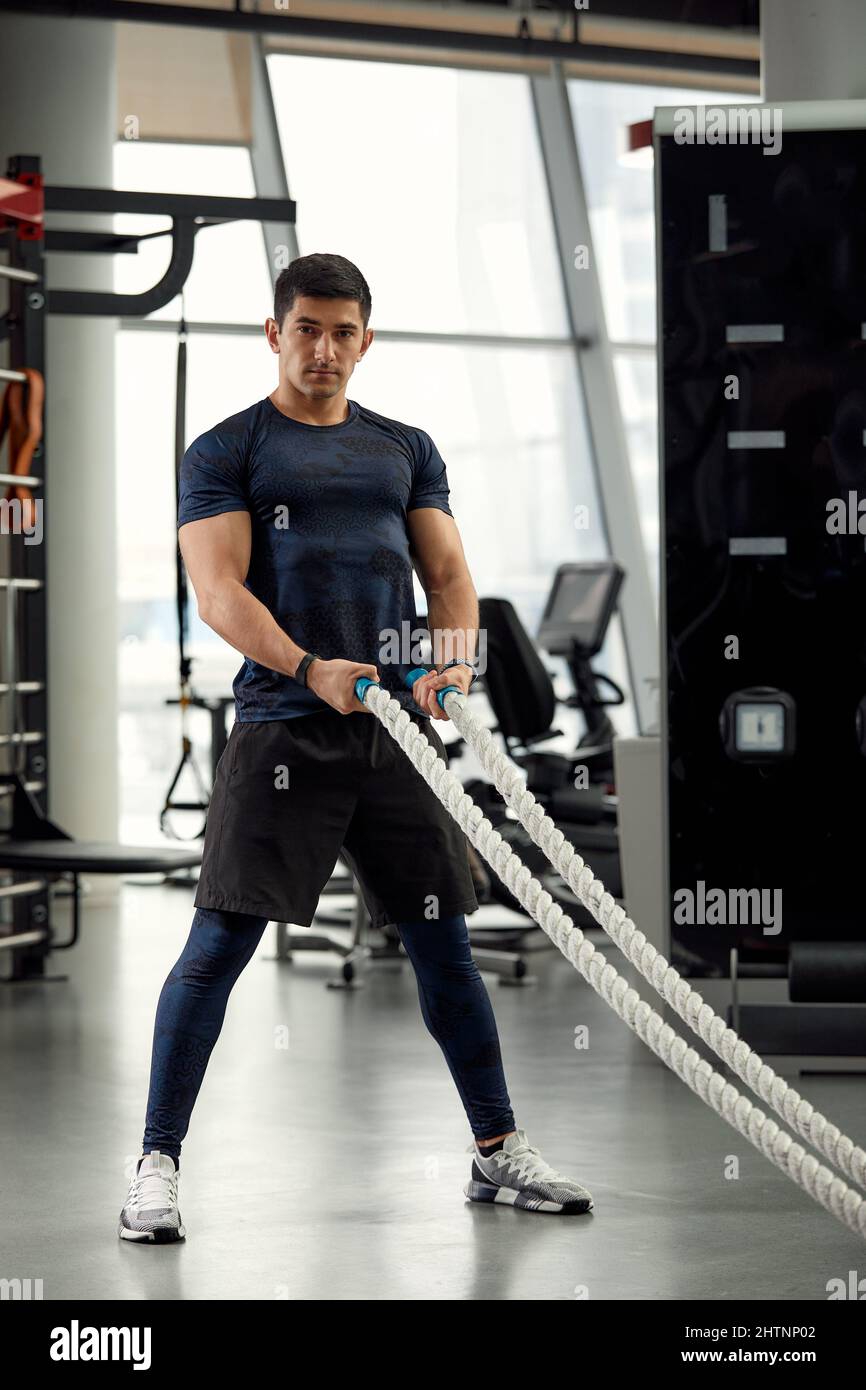 Man sitting on his toes holding a pair of battle ropes for workout. guy ...