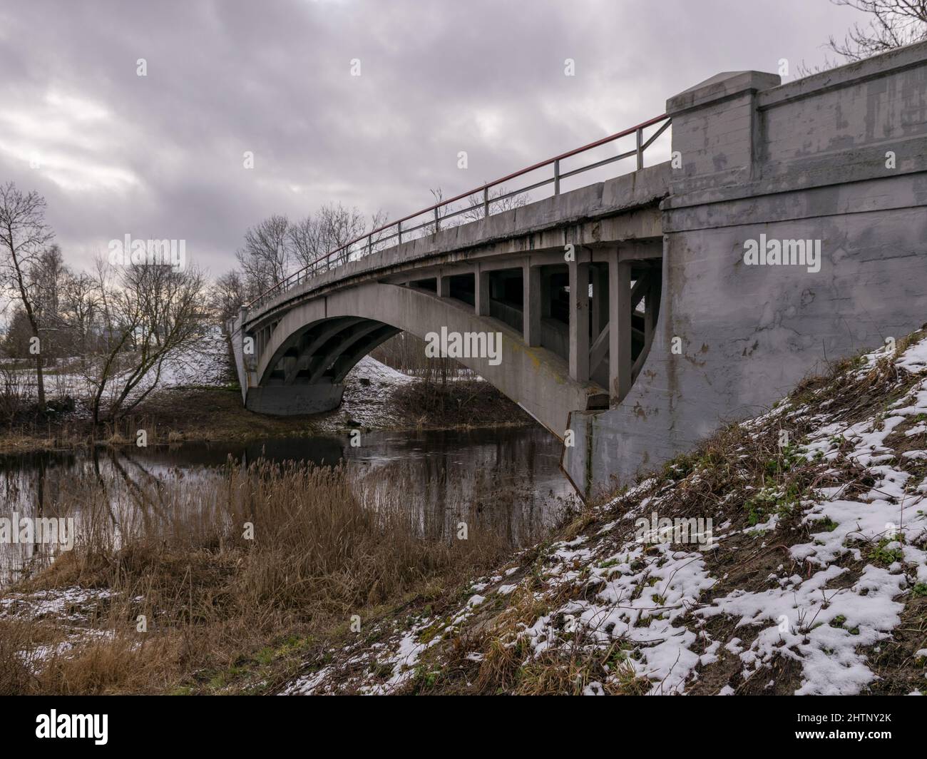 concrete arched bridge over a small and wild river, overgrown with ...