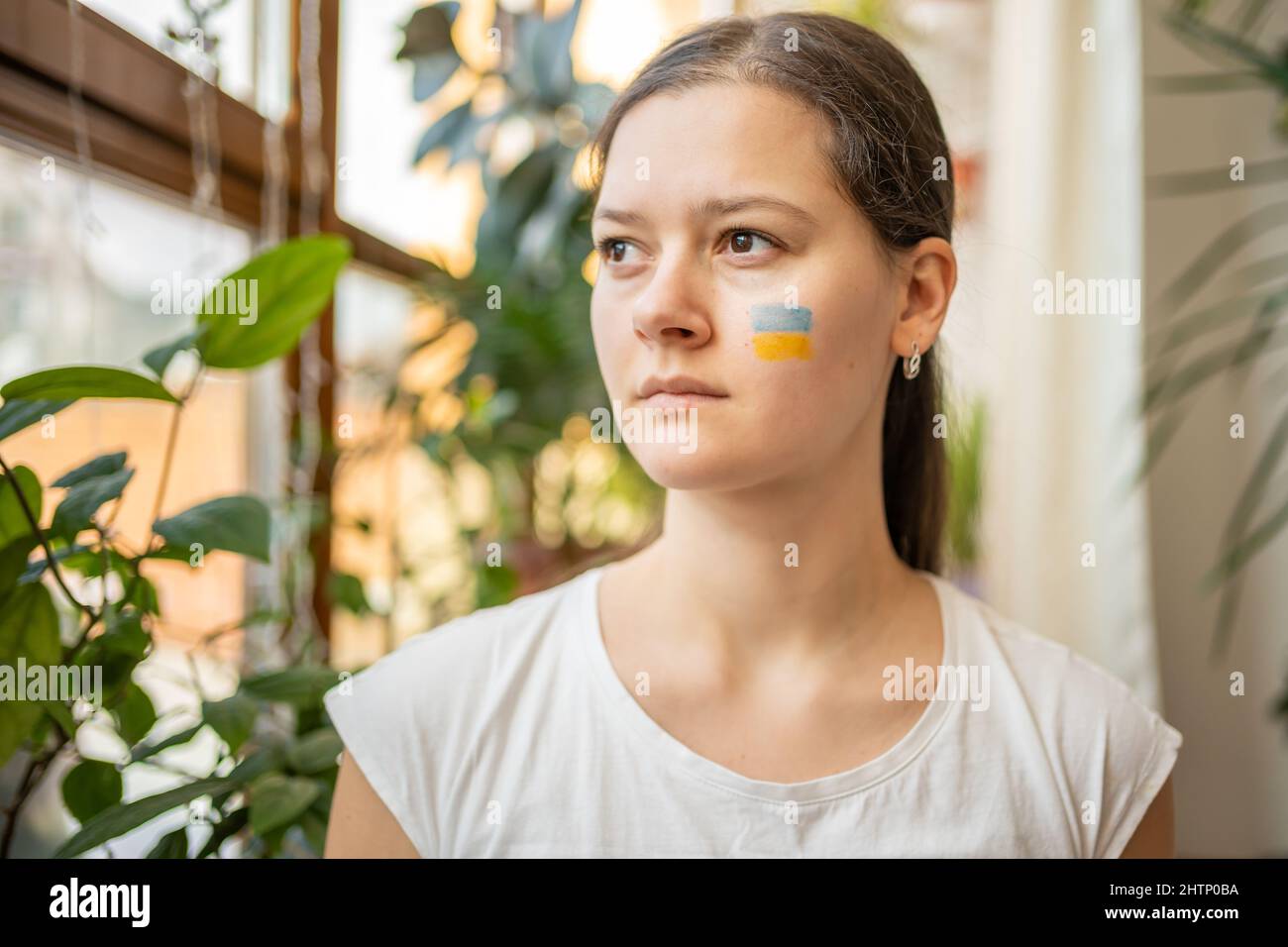 A sad young Ukrainian girl with the flag of Ukraine on her face is ...