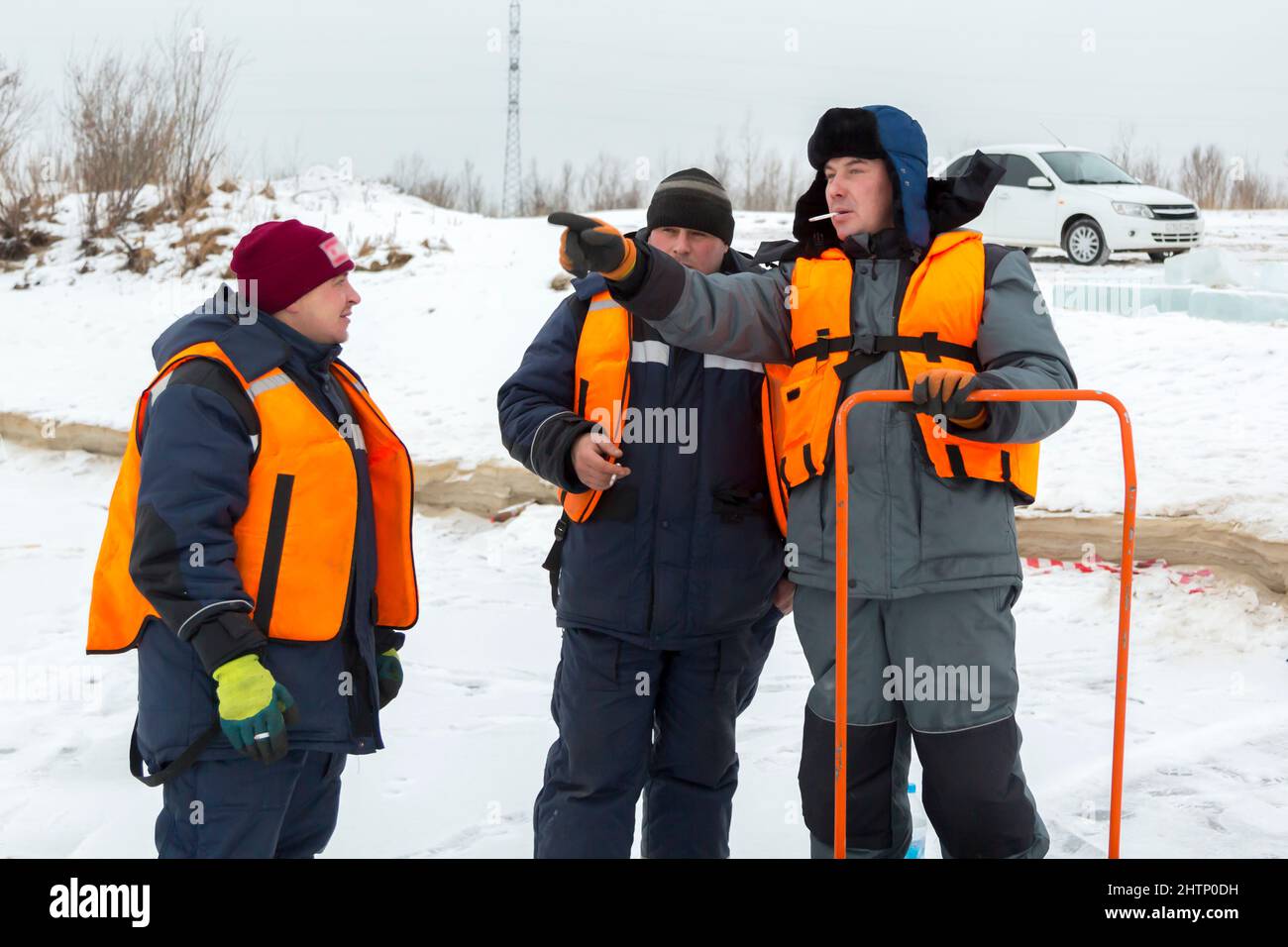 Workers fitters in orange life jackets on the ice of a frozen lake on a ...