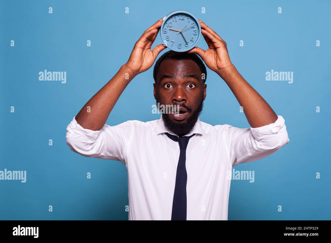 Portrait of stressed office worker holding alarm clock over head ...