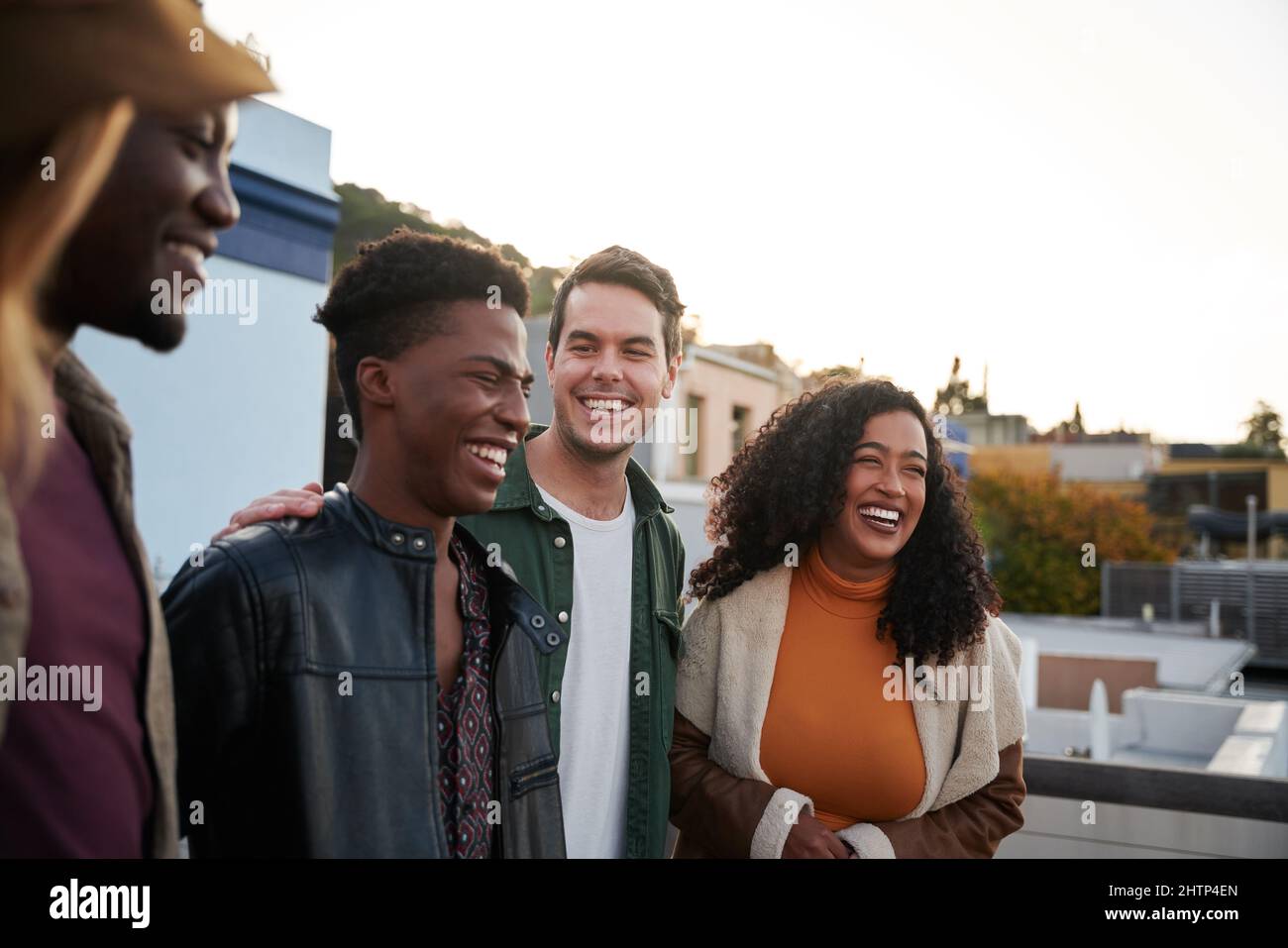 Trendy, diverse group of friends standing together laughing on rooftop ...