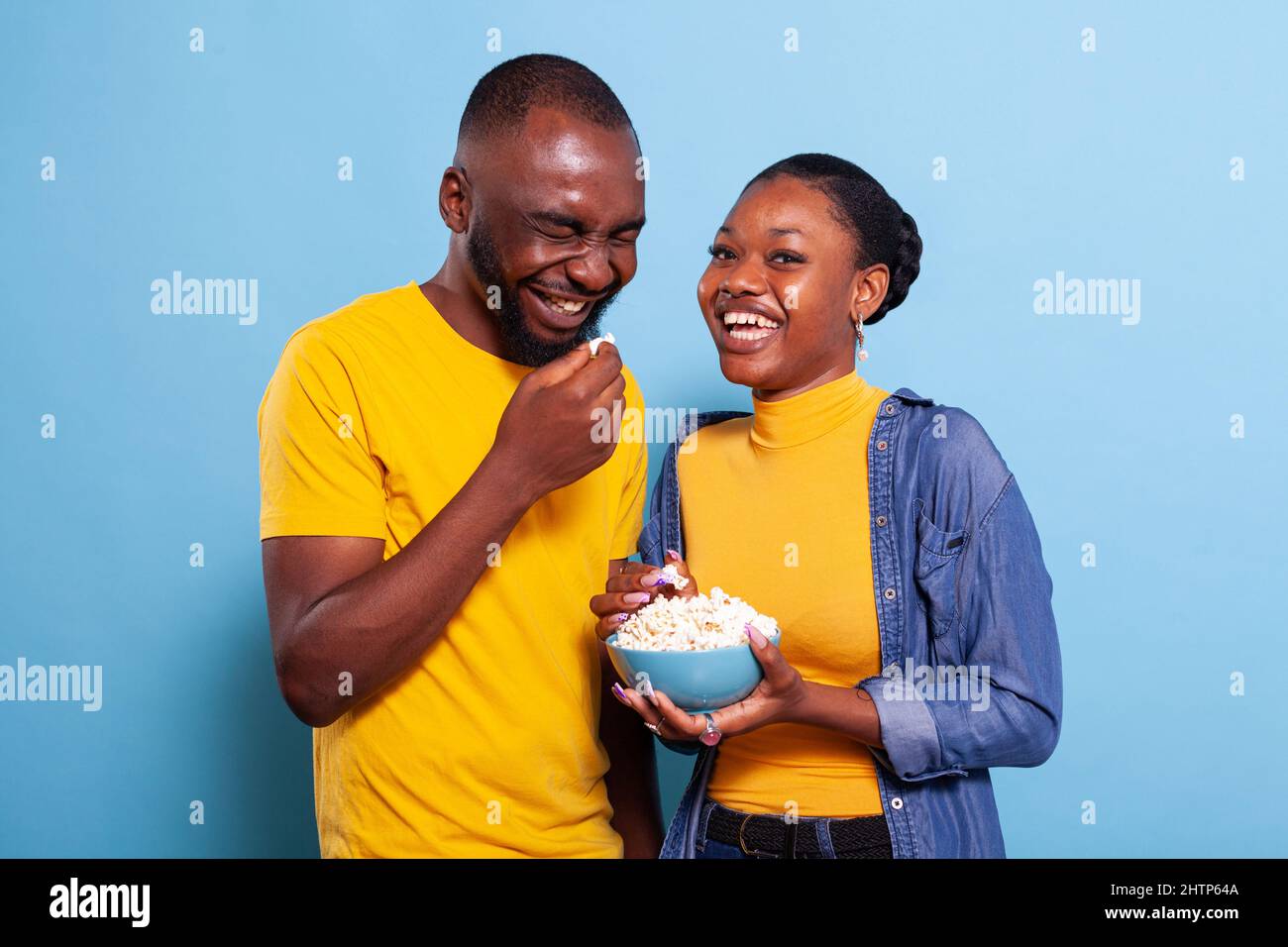 Amused couple watching comedy film on tv and having snack over blue ...