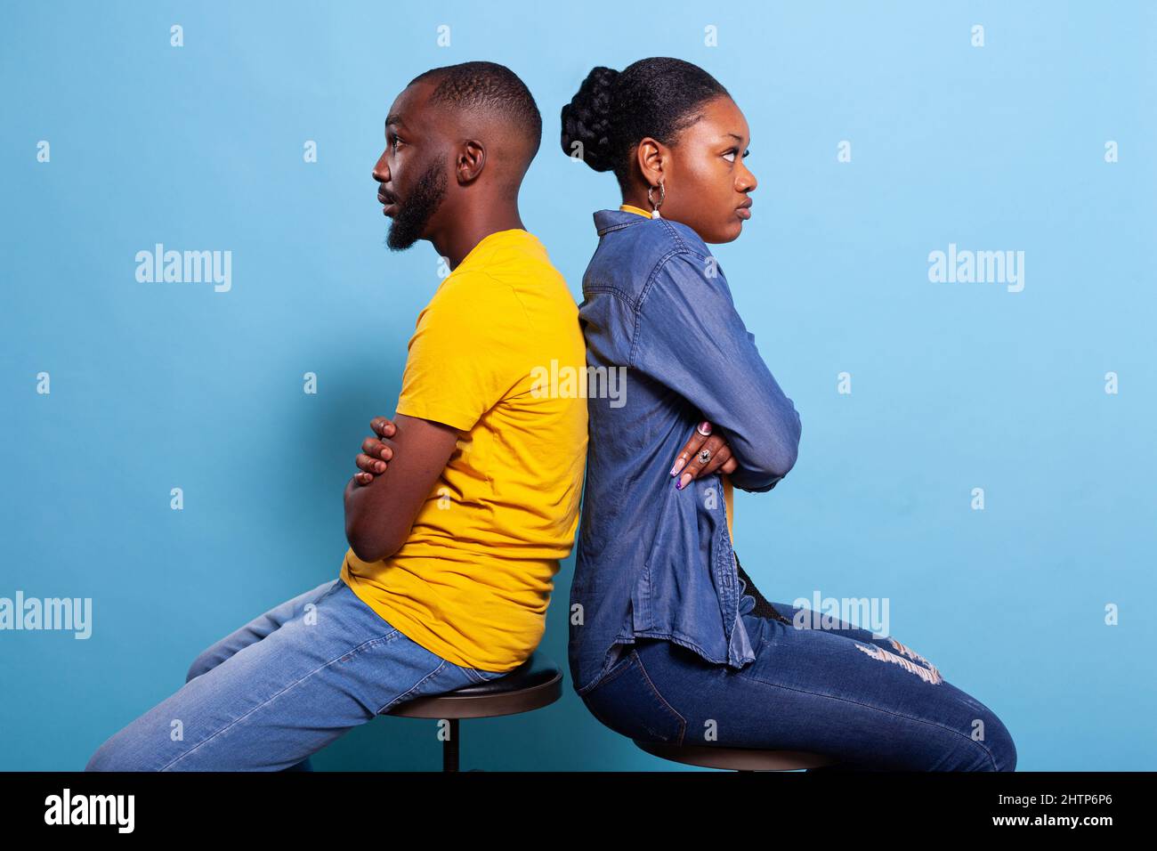Annoyed people sitting back to back with arms crossed in studio ...
