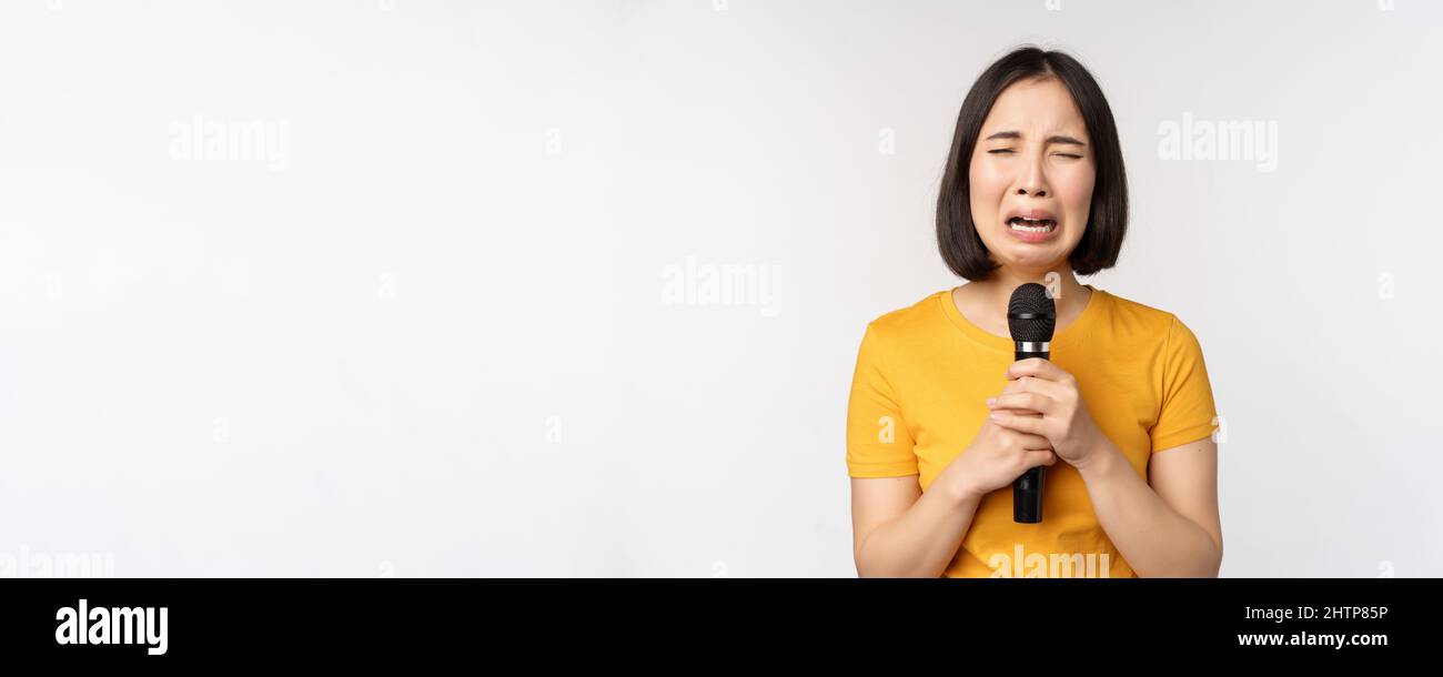 Crying asian girl singing heartbroken in microphone, holding mic and ...