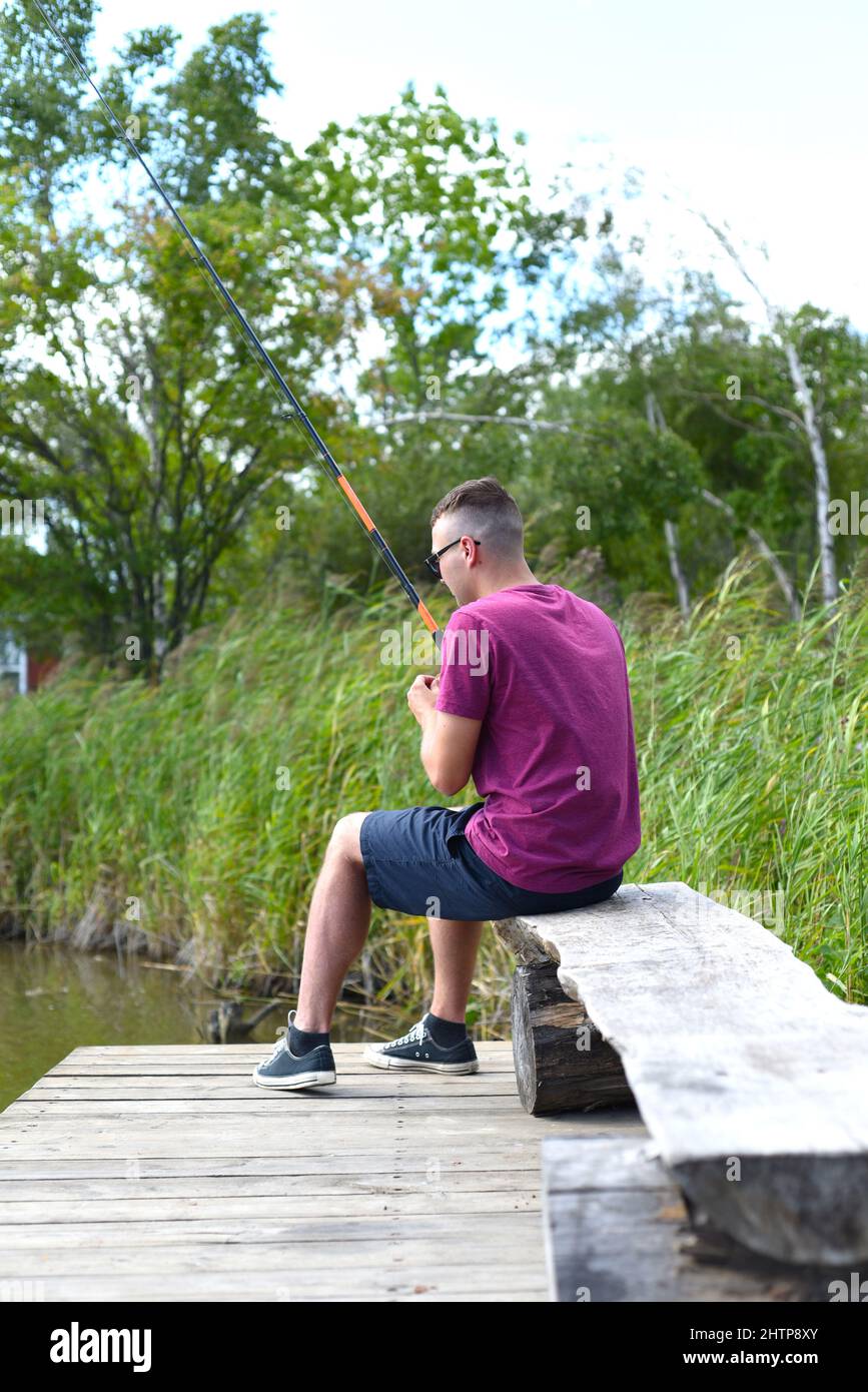 Young fisherman sitting on wooden pier, fishing in the lake. he holding ...