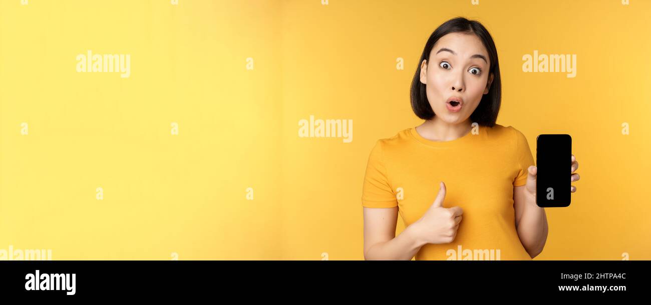 Excited asian woman showing mobile phone screen, thumbs up, like smth ...