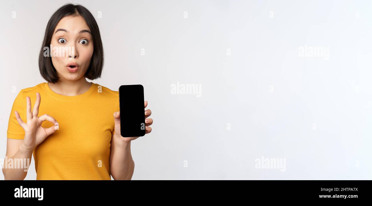 Excited asian girl showing mobile phone screen, okay sign, recommending ...