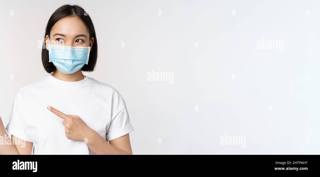 Young korean woman in medical face mask pointing fingers left and ...