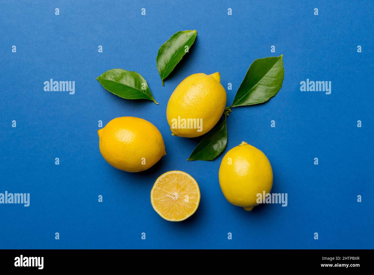Many fresh ripe lemons with green leaves on colored background, top ...