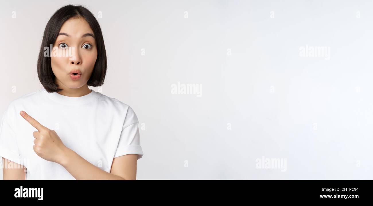 Close up of young japanese woman smiling, pointing finger left at copy ...