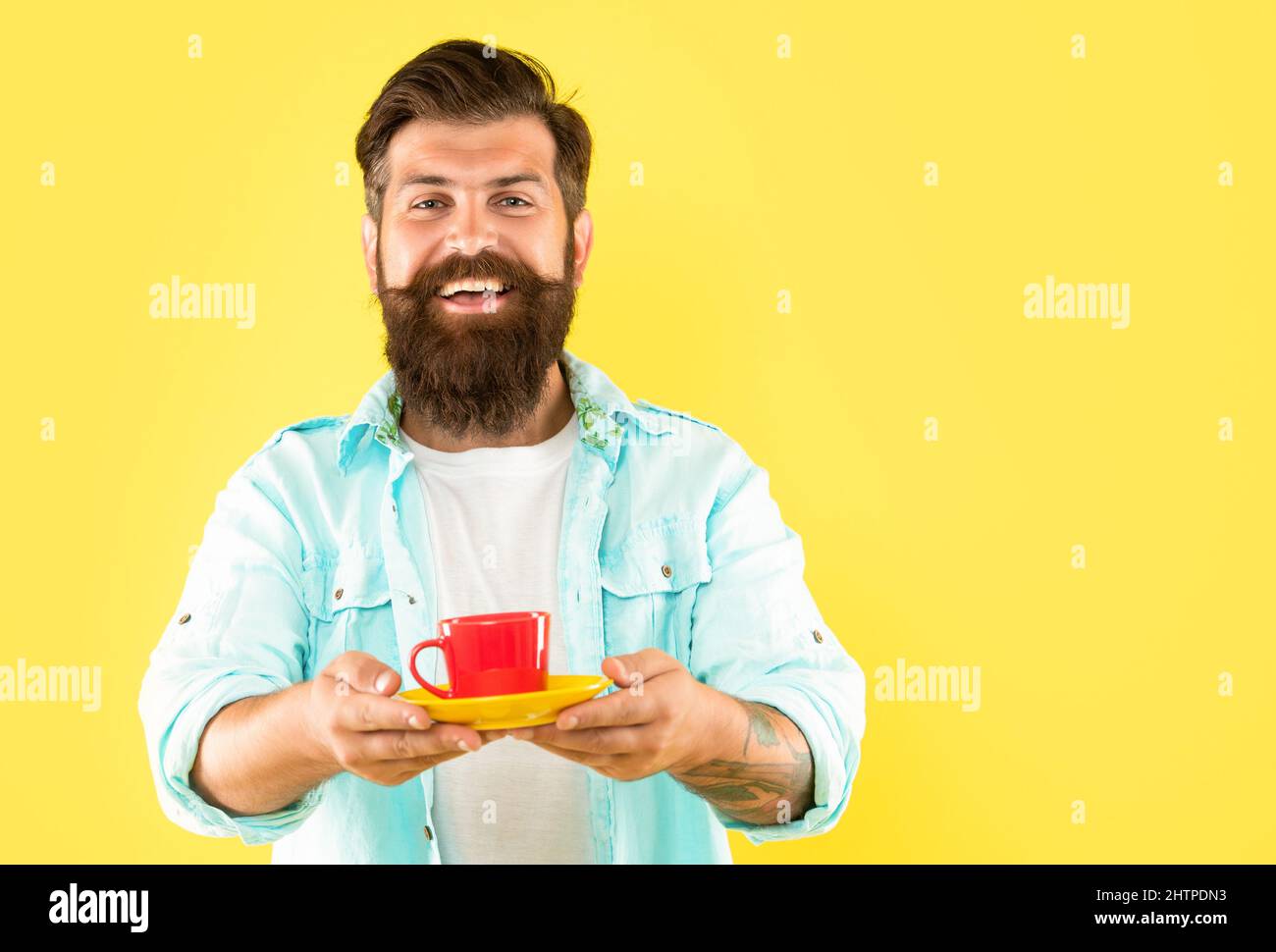 Happy caucasian guy smile giving cup and saucer yellow background copy ...